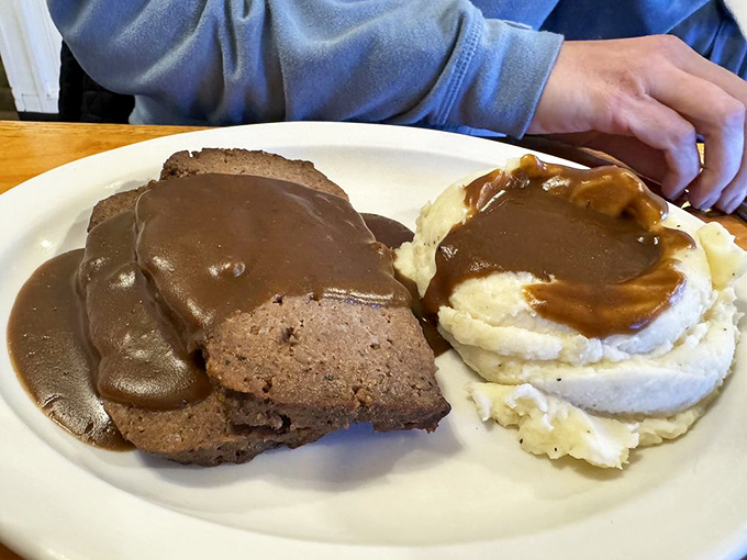 Meatloaf swimming in gravy isn't just comfort food &ndash; it's therapy without the hourly rate, served with mashed potatoes as fluffy as childhood memories.