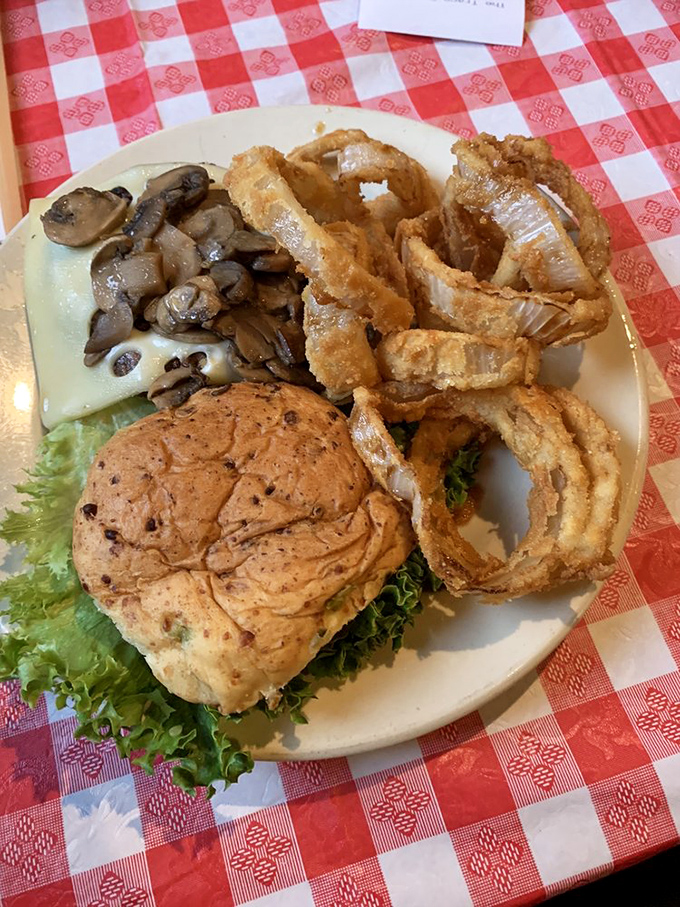 A burger that demands two hands and zero distractions, accompanied by onion rings that could double as golden halos for food angels.