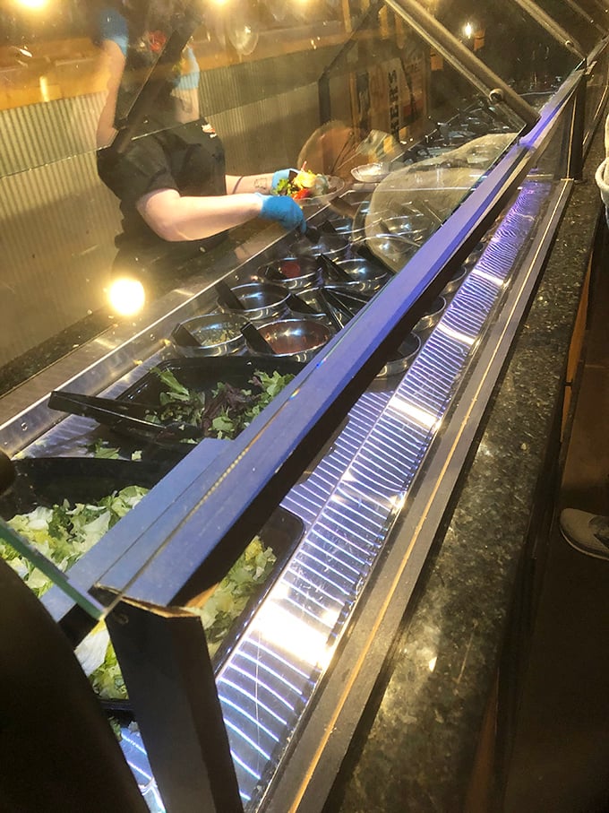 Behind glass, fresh ingredients stand at attention, ready for their salad bar destiny. The gloved hands of preparation add that reassuring touch.
