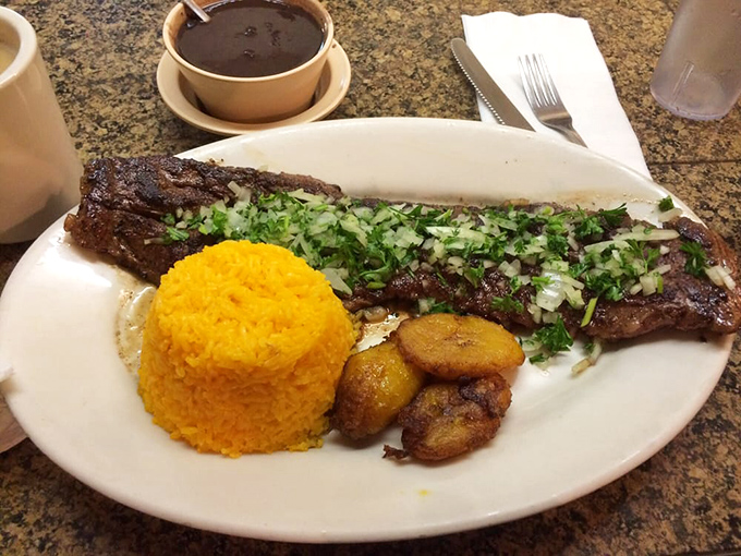 This skirt steak doesn't just sit on the plate—it commands attention. Topped with fresh herbs and flanked by golden rice and plantains, it's carnivore poetry.