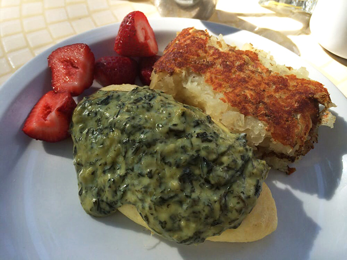 A symphony in green: creamed spinach blankets an English muffin alongside crispy hash browns and fresh strawberries for color contrast.