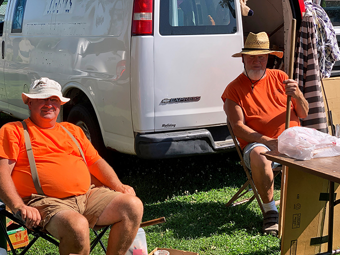 Two vendors in matching orange shirts prove that flea market fashion is all about comfort and visibility.