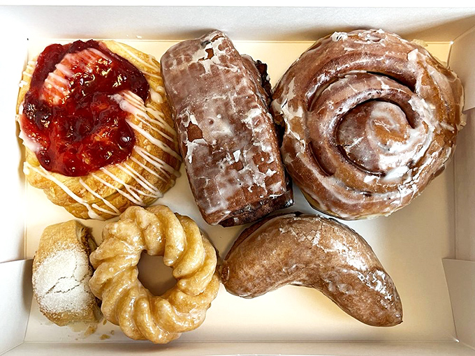 A box of joy containing the Mount Rushmore of pastries: cinnamon roll, fruit danish, powdered donut, and what appears to be a croissant cousin.