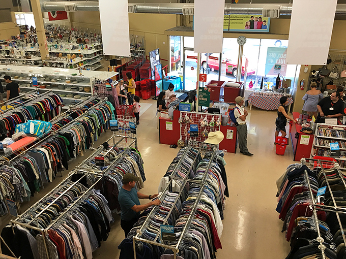From above, the thrift store ecosystem reveals itself. Shoppers migrate between clothing islands, hunting for that perfect vintage find.