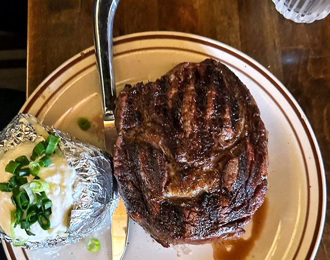 A ribeye that's been kissed by oak fire and finished to perfection, accompanied by a loaded baked potato.