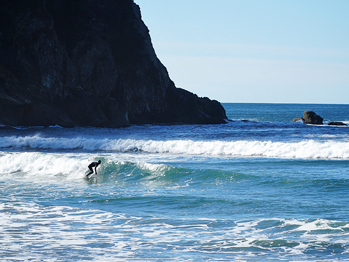 Catching Oregon's liquid gold – a lone surfer harnesses the perfect wave while dramatic cliffs create nature's most spectacular stadium.
