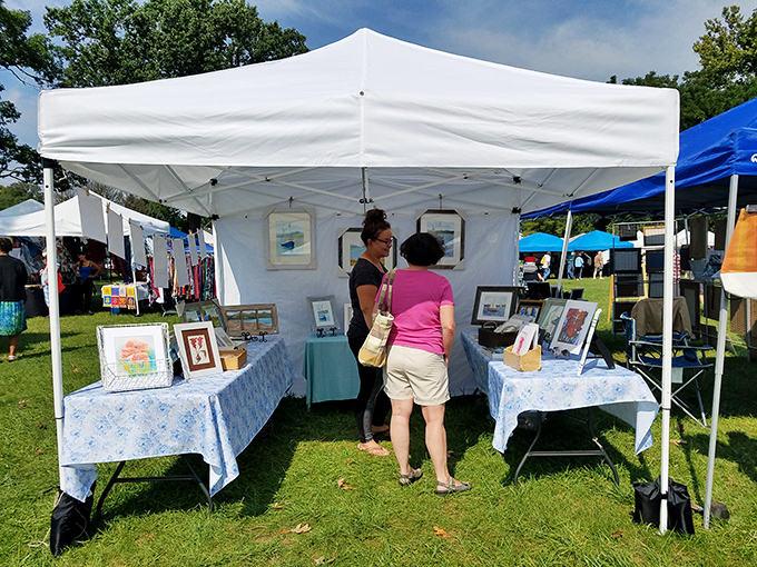 Art lovers gather around framed treasures displayed on grass like an outdoor gallery opening day. 