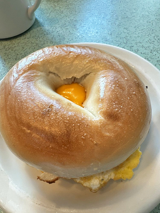 Not just any breakfast sandwich – this bagel creation cradles a sunny egg like it's protecting the morning's most precious treasure.
