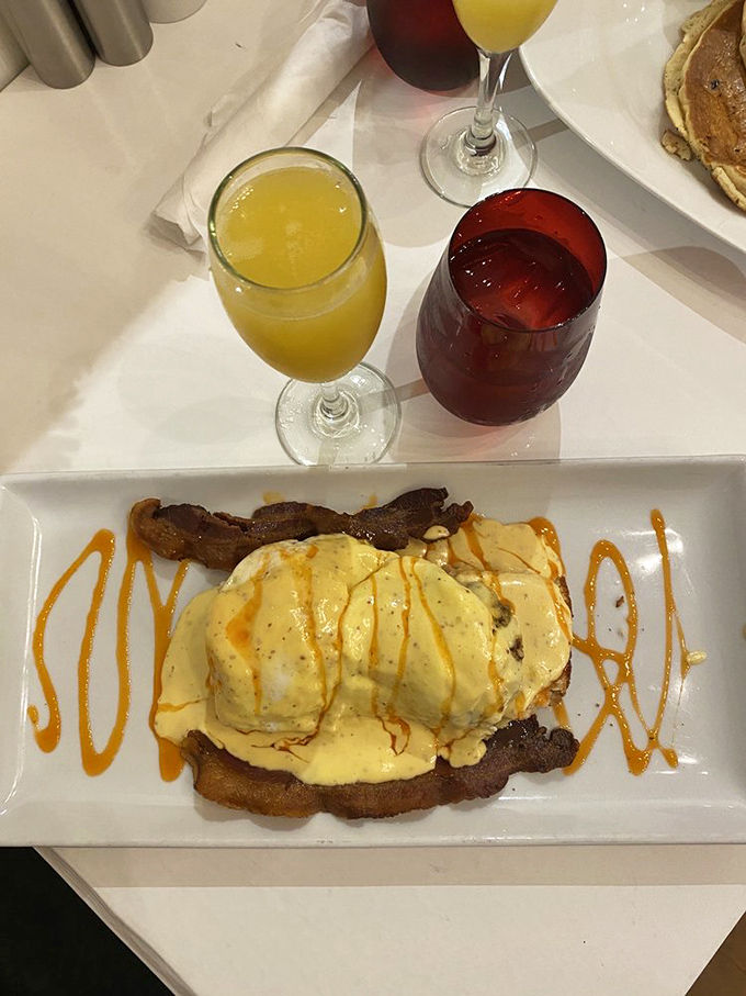Brunch nirvana achieved: eggs draped in hollandaise with a side of perfectly crisped bacon, accompanied by mimosas that practically demand a toast.