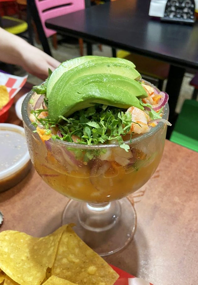 A goblet of ceviche crowned with avocado—ocean freshness and citrus tang in every spoonful, with chips standing by for dipping duty.