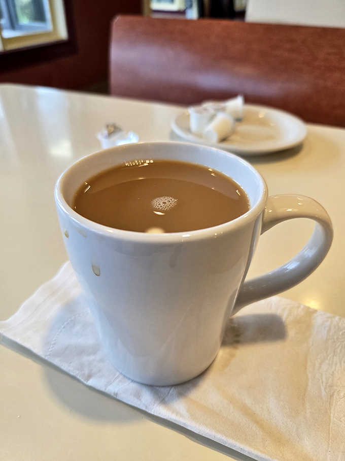 The humble white mug contains liquid ambition, diner coffee that doesn't pretend to be artisanal but absolutely gets the job done.