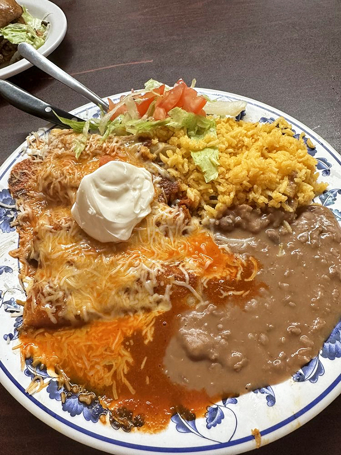 Enchiladas swimming in vibrant sauce, crowned with melted cheese and accompanied by the holy trinity: rice, beans, and a dollop of sour cream.