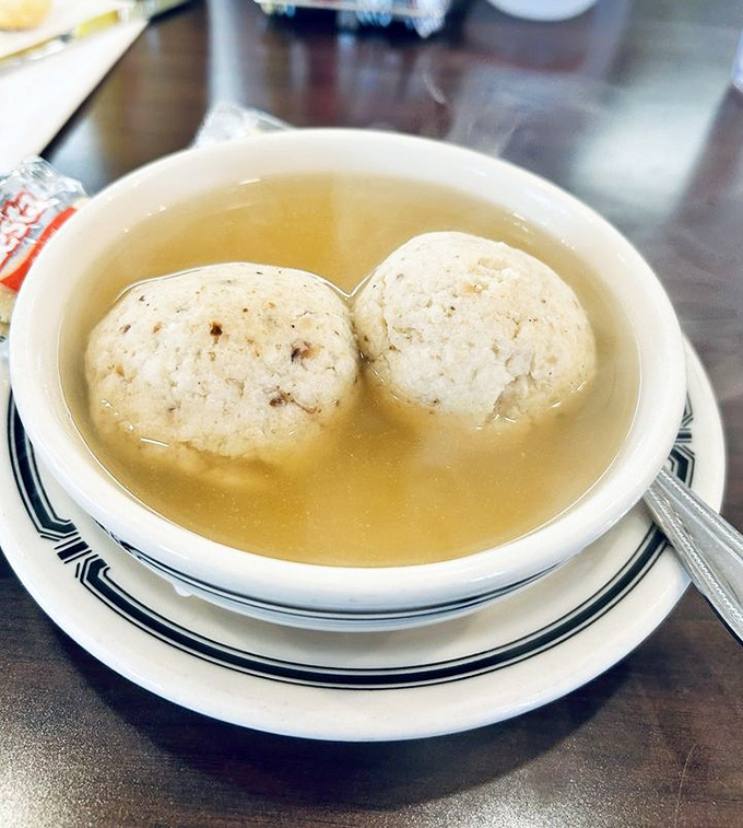 Two perfect matzo balls floating in golden broth like edible planets in a delicious universe. Jewish penicillin at its most comforting.