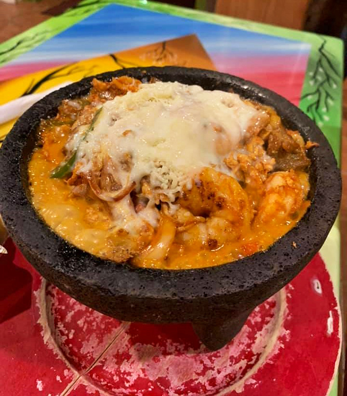 The molcajete arrives still bubbling like a volcanic masterpiece, cheese stretching skyward as if trying to escape its delicious stone prison.