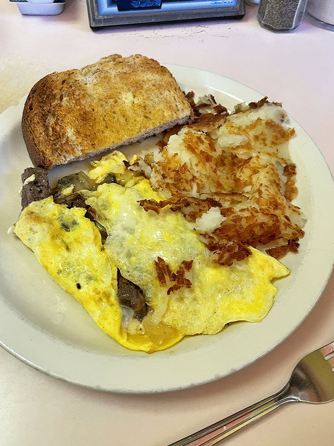 Breakfast architecture at its finest: layers of fluffy eggs, vegetables, and melted cheese with crispy hash browns as the foundation.