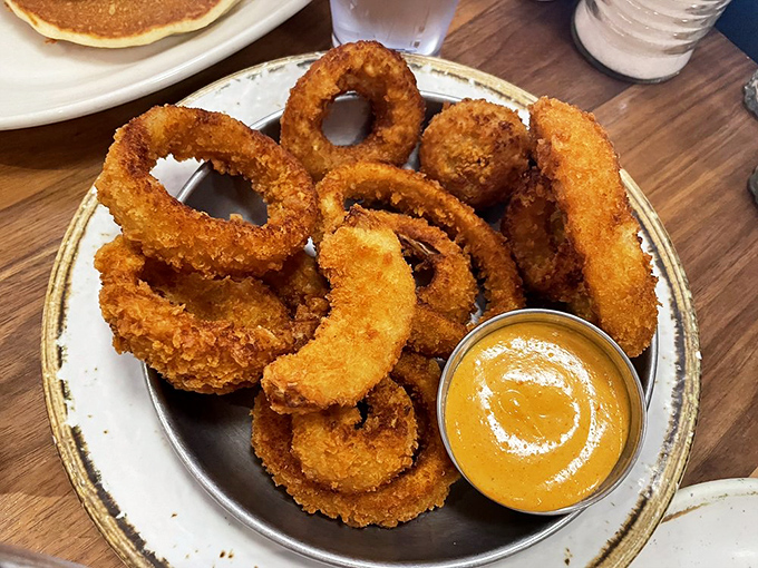 Onion rings stacked like golden halos, each one perfectly crisp and ready for dunking in that sunshine-colored dipping sauce.