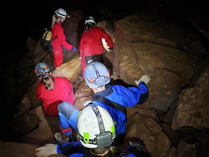 Modern-day explorers navigate by headlamp through passages that remained hidden for centuries. Indiana Jones would approve of these red suits.