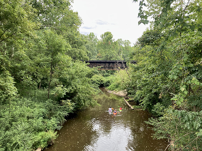 The Eno River flows gently beneath a canopy of trees, offering kayakers and tubers a refreshing escape from summer heat.