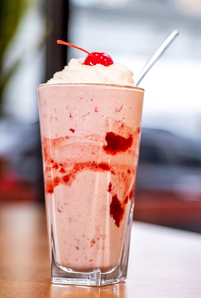 This strawberry milkshake isn't just a drink—it's dessert in disguise, wearing a whipped cream hat and cherry beret.