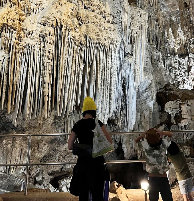 Visitors stand in awe before a wall of delicate formations. That yellow beanie will come in handy&mdash;cave exploration is the original "hard hat required" adventure.