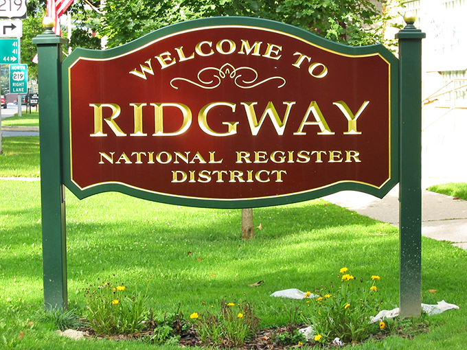 "Welcome to Ridgway National Register District"—a sign that doesn't just mark location but announces you've entered somewhere special. Those manicured flowers are the town's way of rolling out the green carpet.