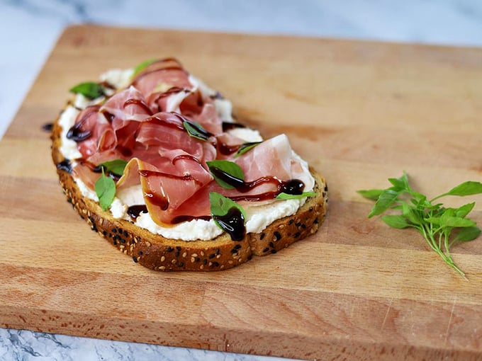 An open-faced sandwich that's dressed better than most people at Sunday brunch. Prosciutto, fresh herbs, and cheese playing together like old friends.