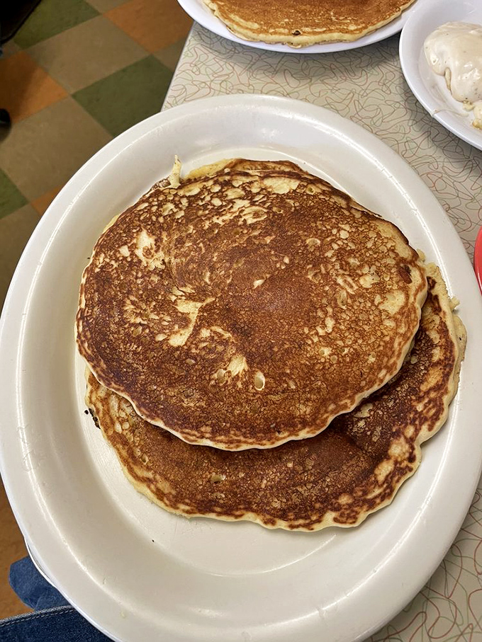 Pancakes so perfectly golden they belong in Fort Knox, stacked high enough to cast a shadow across your breakfast expectations.