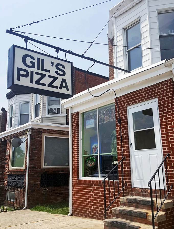 Red brick, white siding, and a window full of neon - Gil's Pizza keeps it old-school in the best possible way.