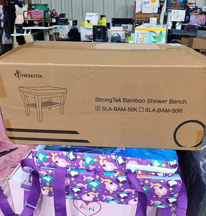 Home improvement gold: a bamboo shower bench still in its box sits atop a colorful children's bag. One person's overstock becomes another's bathroom upgrade.