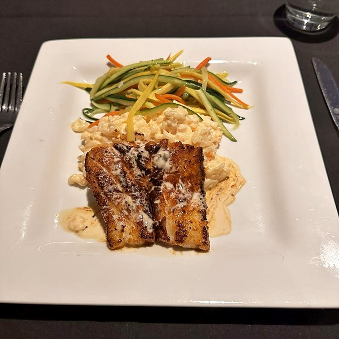 Blackened sea bass perched atop risotto like a culinary crown jewel, with julienned vegetables adding both color and crunch to this royal feast.