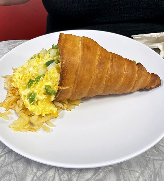 A croissant breakfast sandwich reinvented as edible architecture &ndash; eggs and veggies nestled in golden-brown pastry with hash browns standing guard.