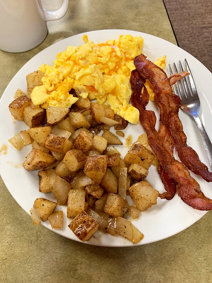 The breakfast trinity: crispy potatoes, scrambled eggs, and bacon cooked to that perfect point between chewy and crisp. Morning salvation on a white plate.