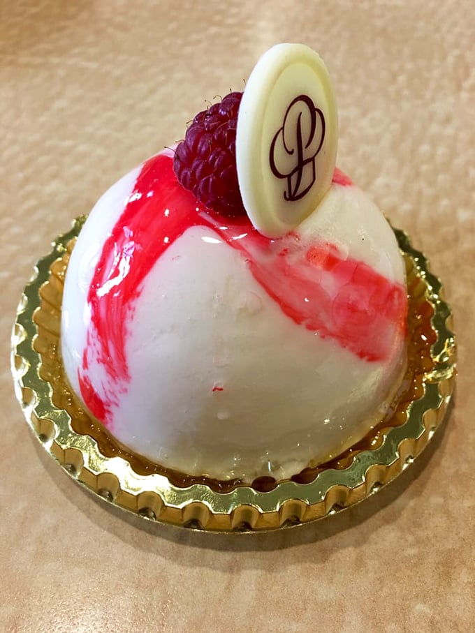 This dome-shaped masterpiece isn't just dessert&mdash;it's architecture. The raspberry and white chocolate glaze create edible modern art on a gold pedestal.