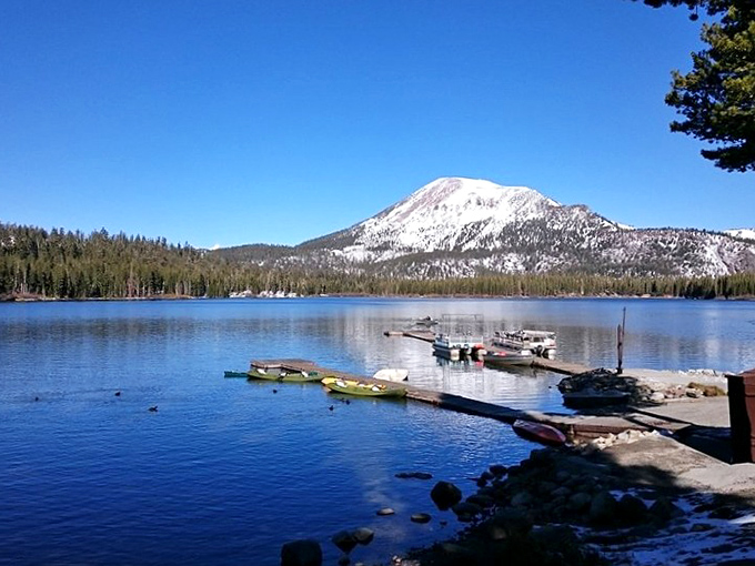 Lake Mary's mirror-like perfection: Mammoth Mountain stands sentinel over calm waters where boats wait patiently for the next fishing adventure.
