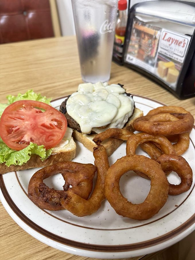 A burger wearing a melted cheese blanket, escorted by onion rings so perfectly golden they deserve their own trophy. Diet plans come here to die.