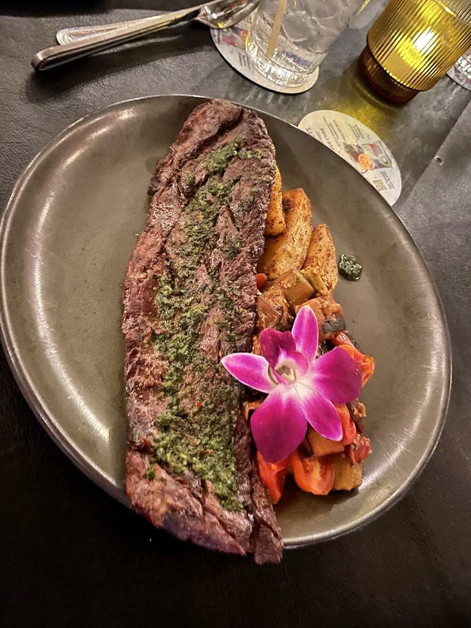 This skirt steak wearing its chimichurri crown sits majestically beside roasted vegetables. The orchid isn't just garnish&mdash;it's applauding the chef's achievement.