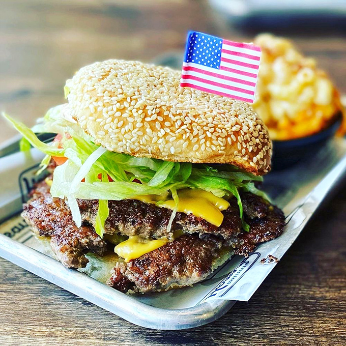 The flag isn't just patriotic&mdash;it's marking the conquest of burger territory. Sesame seed bun crowning a masterpiece of meat and toppings.