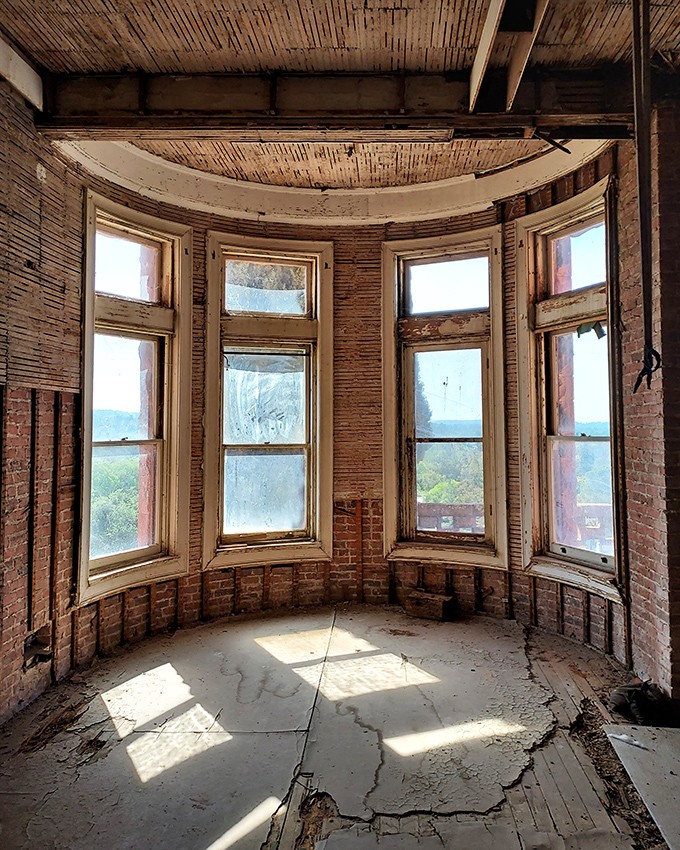 Sunlight streams through weathered windows in this curved alcove, nature's spotlight illuminating decades of peeling paint and architectural details rarely seen in American buildings.