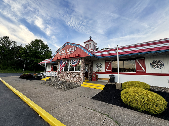The red-roofed Dutch Pantry stands like a beacon of comfort food salvation along the Pennsylvania highway, promising homestyle goodness within those patriotic-trimmed walls.