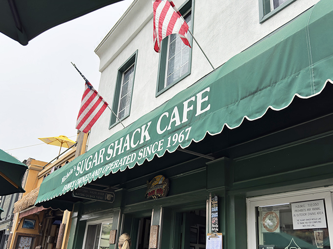 The iconic green awning of Sugar Shack Cafe stands as a beacon of breakfast hope on Huntington Beach's Main Street, American flags fluttering above like culinary patriotism.