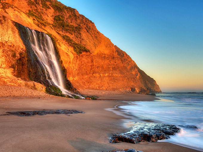 Nature's ultimate magic trick: a 40-foot waterfall that plunges directly onto the beach, catching golden hour light like it's auditioning for National Geographic.