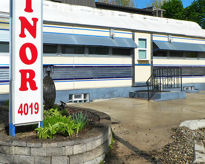 The classic silver exterior of Lawrence Park Dinor gleams in the sunlight, a time capsule of Americana with its distinctive blue trim and welcoming garden.