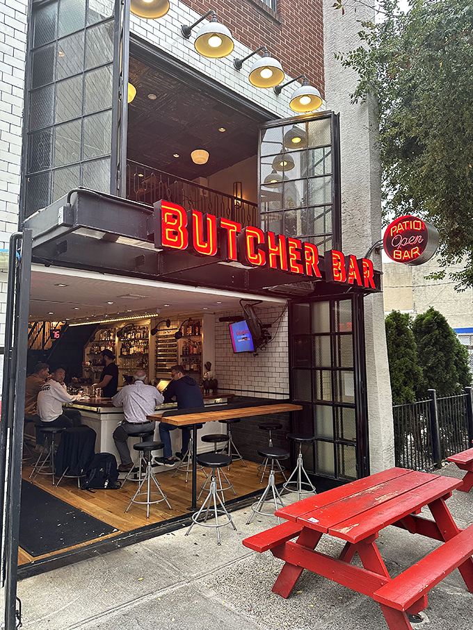 The neon-red Butcher Bar sign glows like a carnivorous lighthouse, beckoning hungry travelers through Philadelphia's evening darkness.
