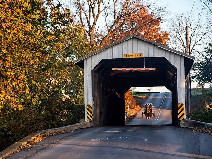 The classic white and red entrance of Eshleman's Mill Covered Bridge stands like a portal to simpler times, complete with an Amish buggy making its way through.