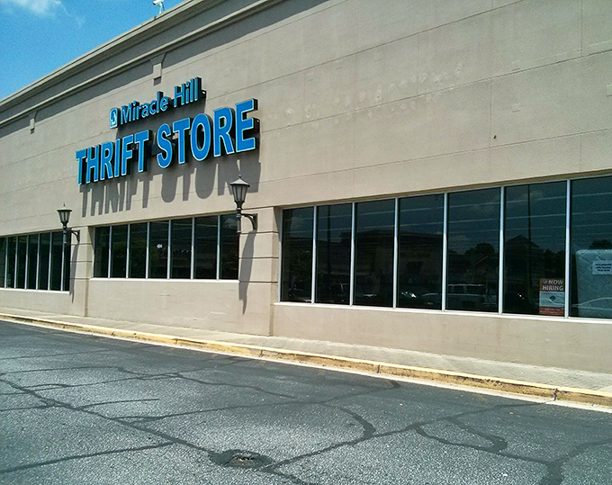The iconic blue signage of Miracle Hill Thrift Store stands out against the beige exterior like a beacon calling to bargain hunters everywhere.