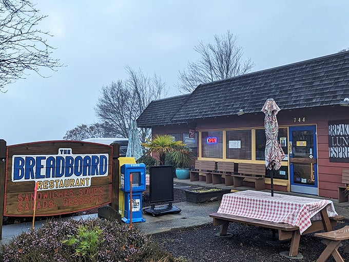 The rustic cabin exterior of The Breadboard promises comfort food nirvana. That red-checkered tablecloth isn't just decoration&mdash;it's foreshadowing.