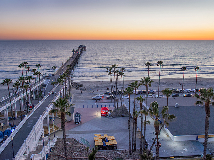 Sunset perfection at Oceanside Pier, where palm trees stand like nature's exclamation points against the golden horizon. This wooden wonder stretches nearly 2,000 feet into the Pacific.
