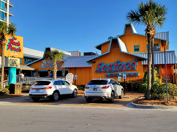 The bright orange exterior of Back Porch Seafood & Oyster House stands out like a cheerful beacon against Destin's blue sky, promising seafood treasures within.