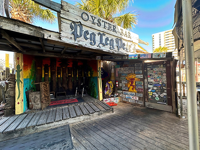 The weathered wooden exterior of Peg Leg Pete's stands like a salty sea captain against Pensacola Beach's blue sky, pirate flags fluttering in welcome.