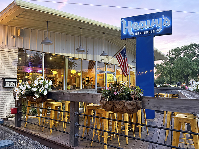 Heavy's blue sign glows like a beacon for burger pilgrims. The charming patio with those signature yellow stools practically whispers, "Sit here, happiness awaits." 